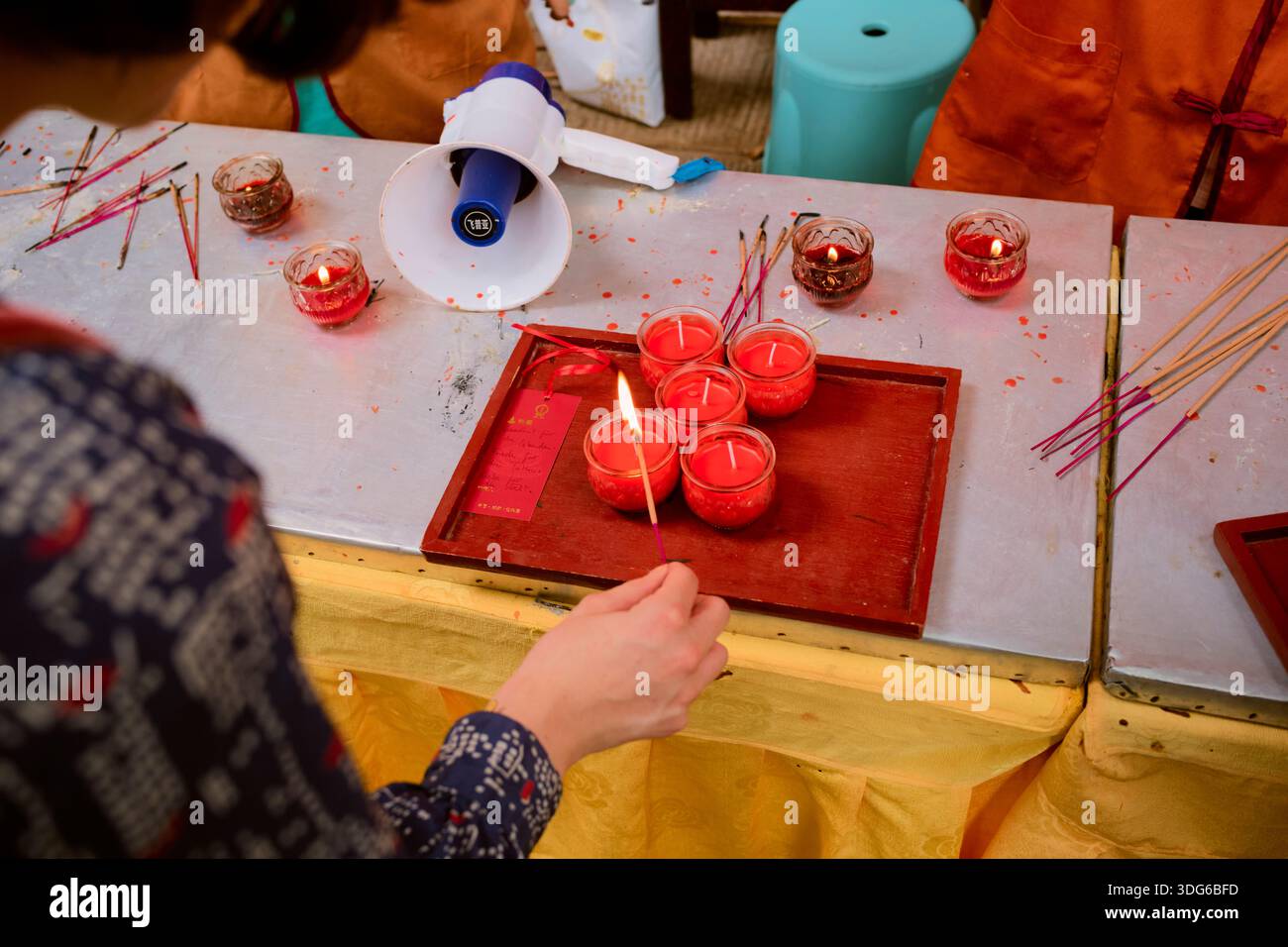 A person lights candles on a tray at a colorful indoor ritual setup ...