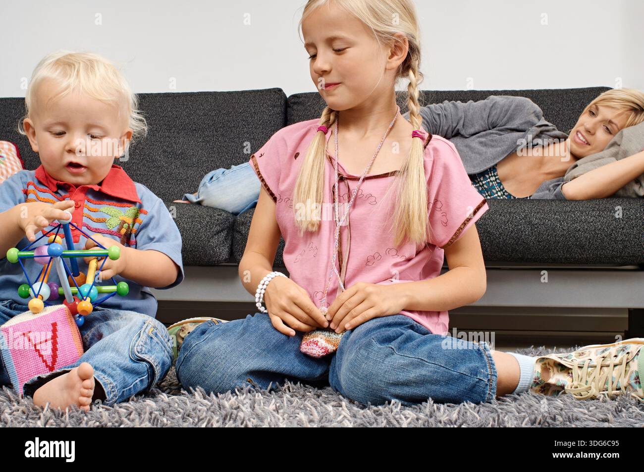 Two children playing on a rug with a woman relaxing on the couch in the ...