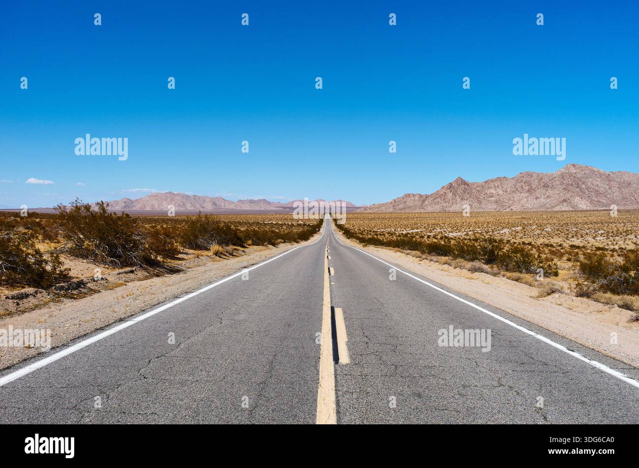 Long desert highway stretches into the horizon under a clear blue sky ...