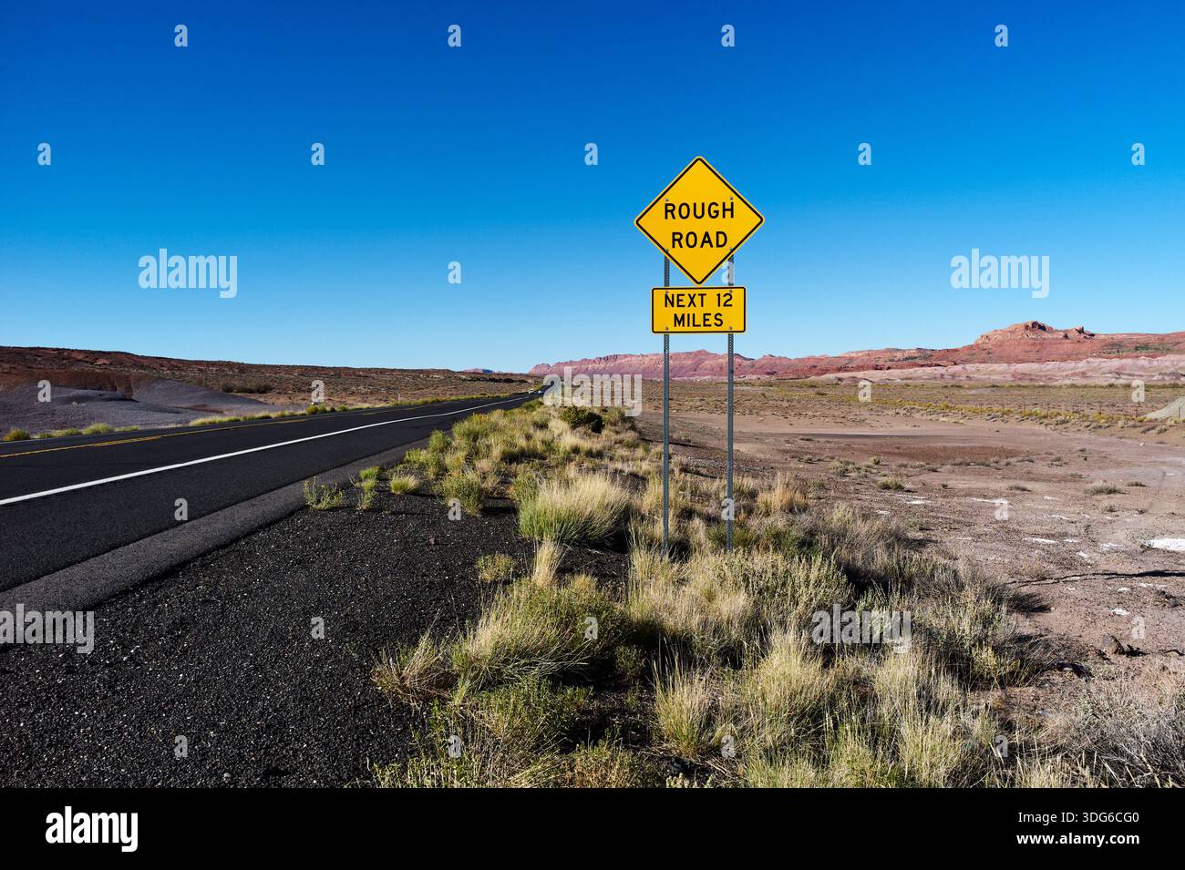 Desert road with rough road sign and distant red cliffs under a clear ...