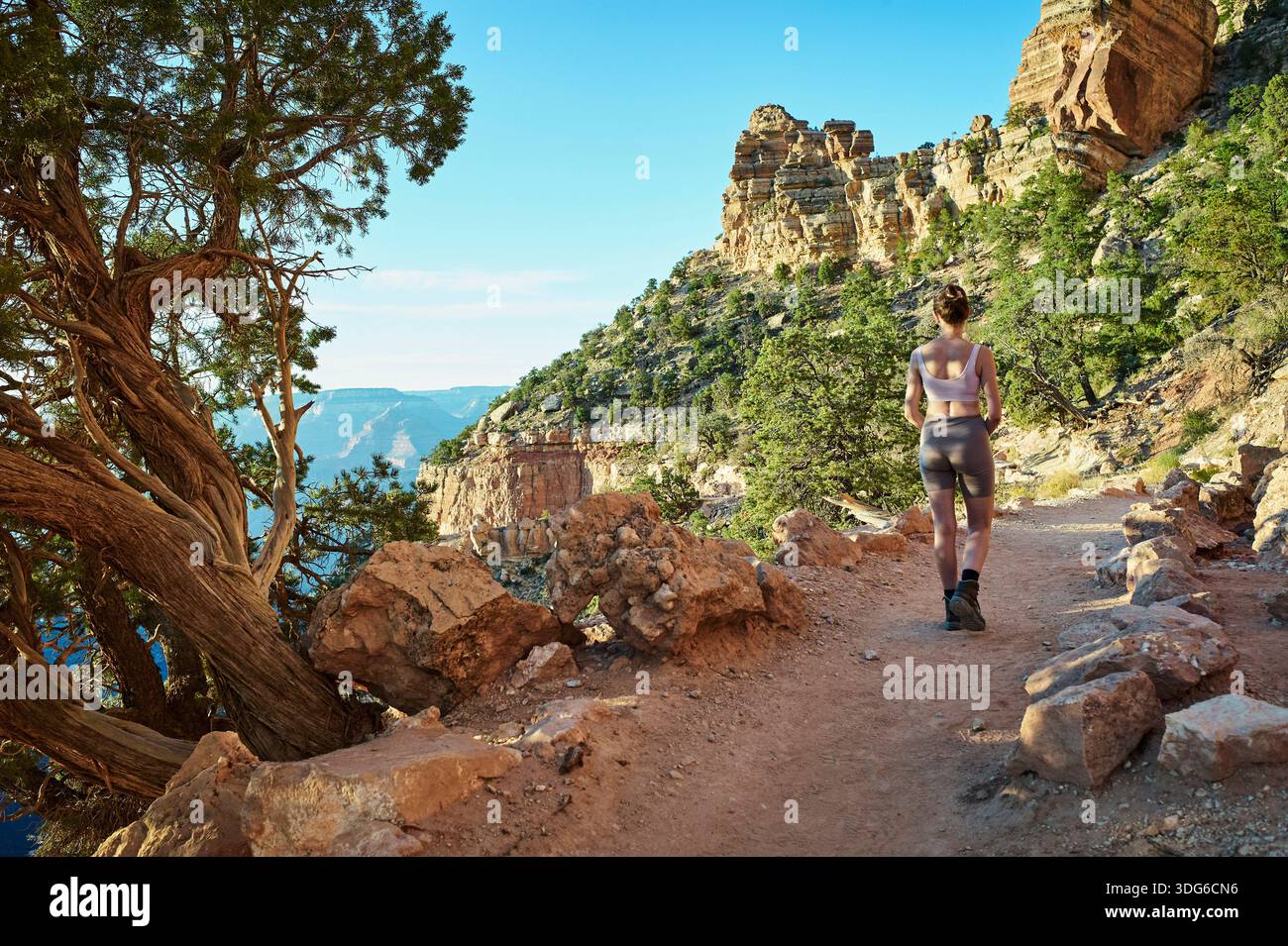A woman hikes along a scenic trail on a rocky mountain under a clear ...