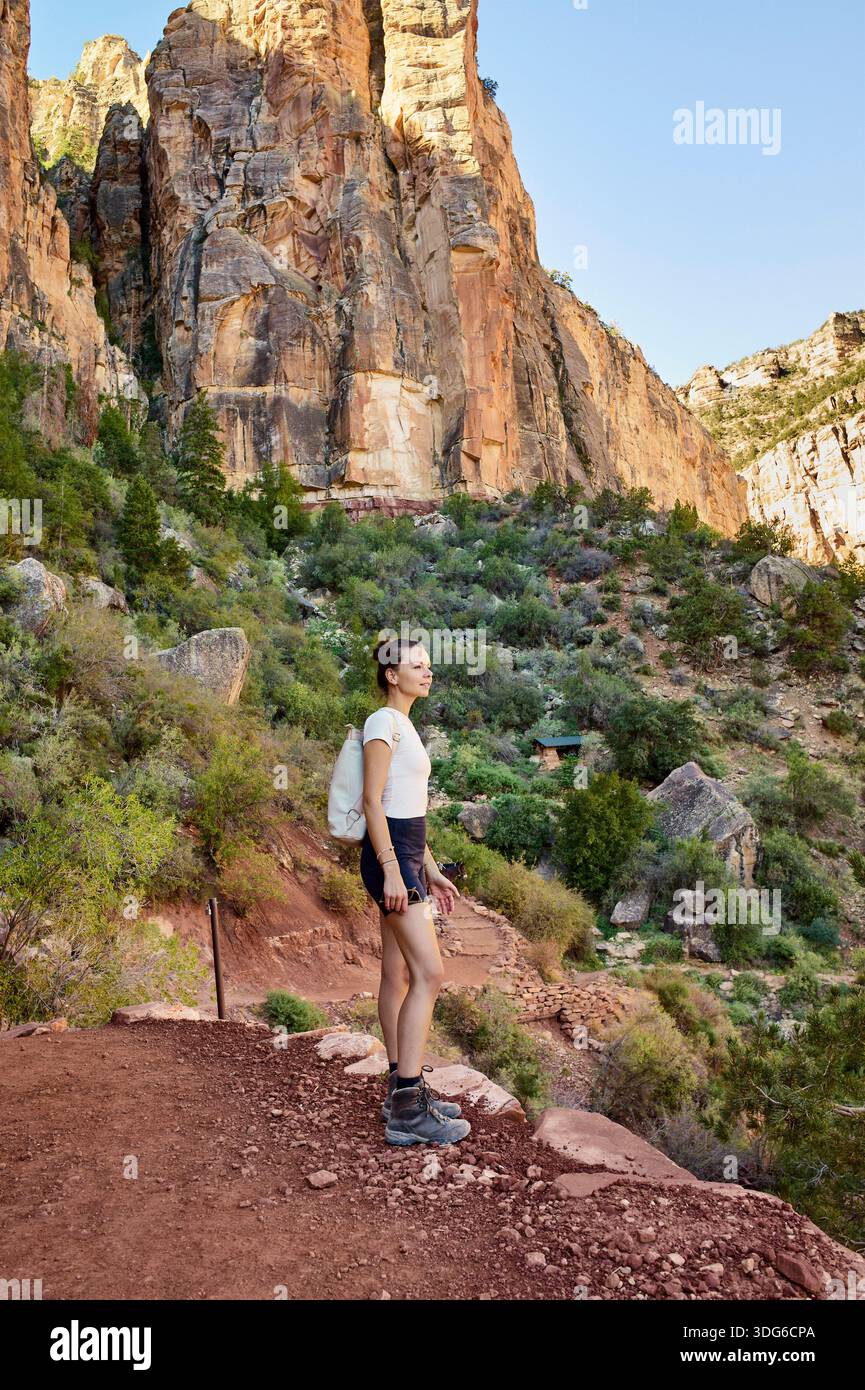 Woman hiking along a scenic rugged trail with towering cliffs under a ...