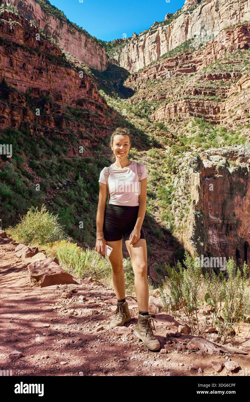 Woman hiking on a sunny canyon trail wearing a white shirt and black ...