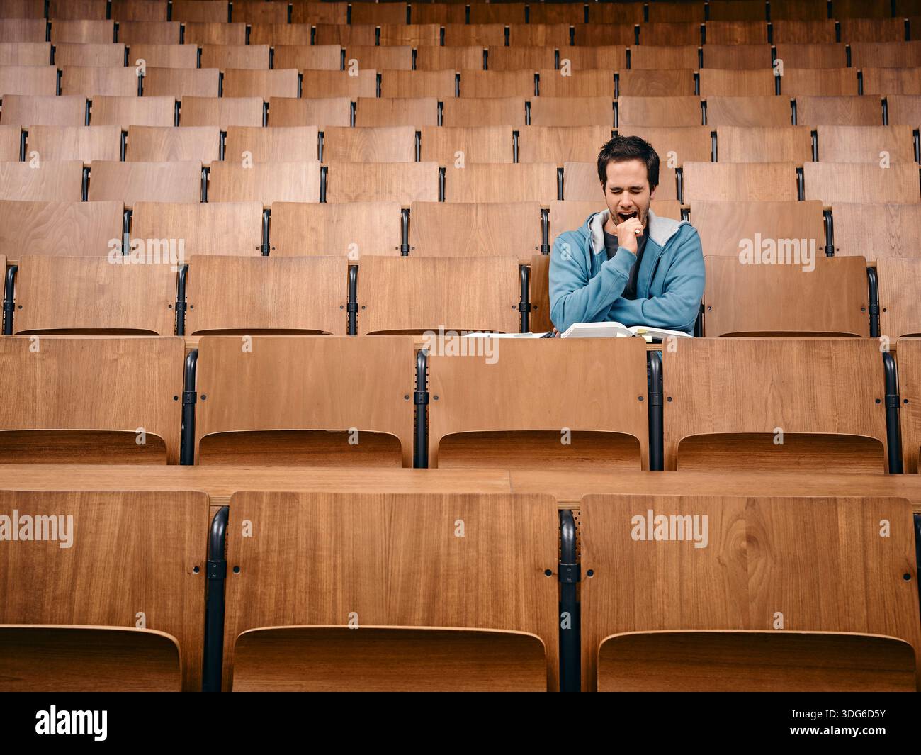 Man in a blue sweater sitting and studying in a large empty wooden ...