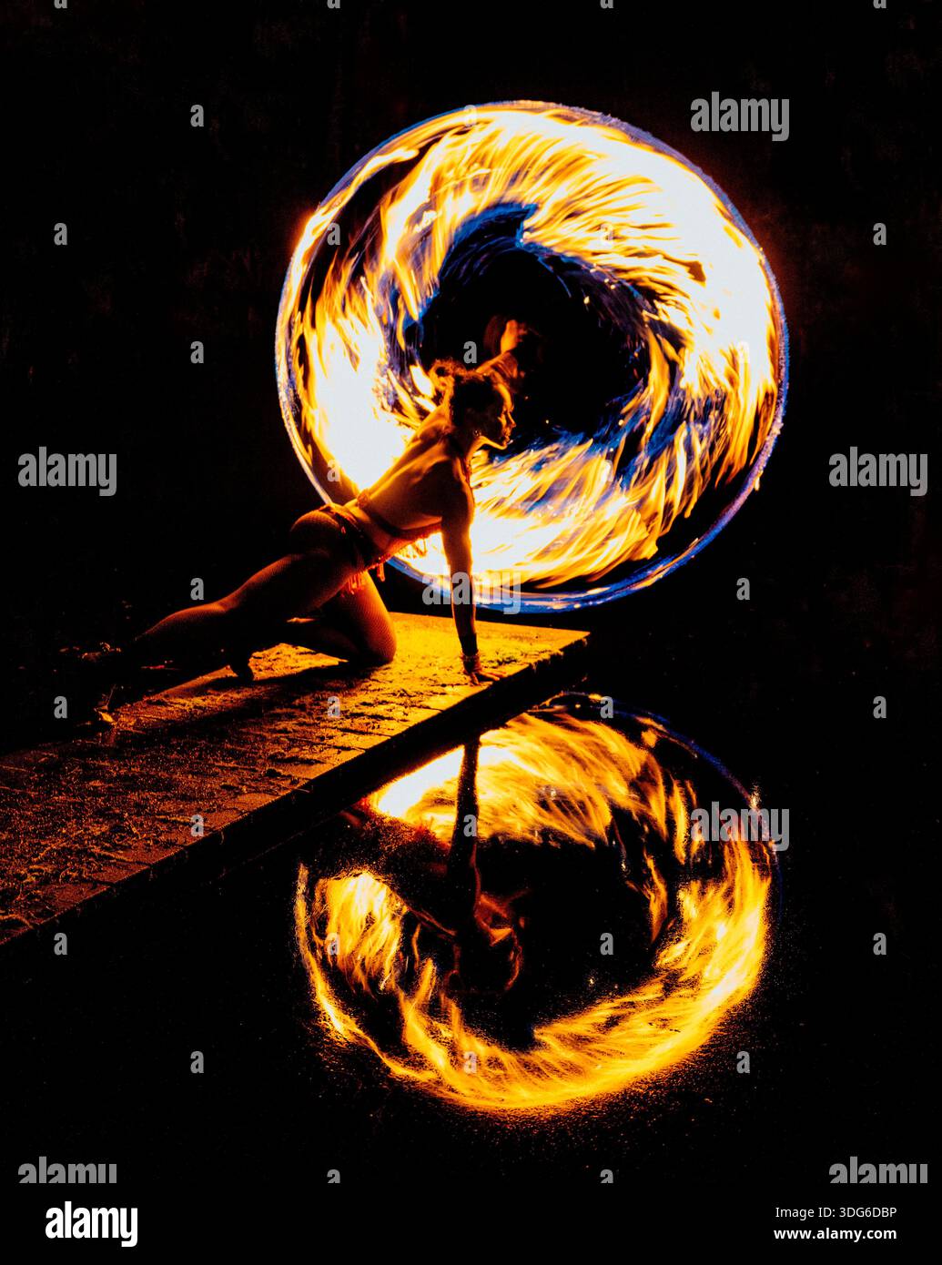 Fire dancer performing with a fire hoop at night, reflecting on water ...