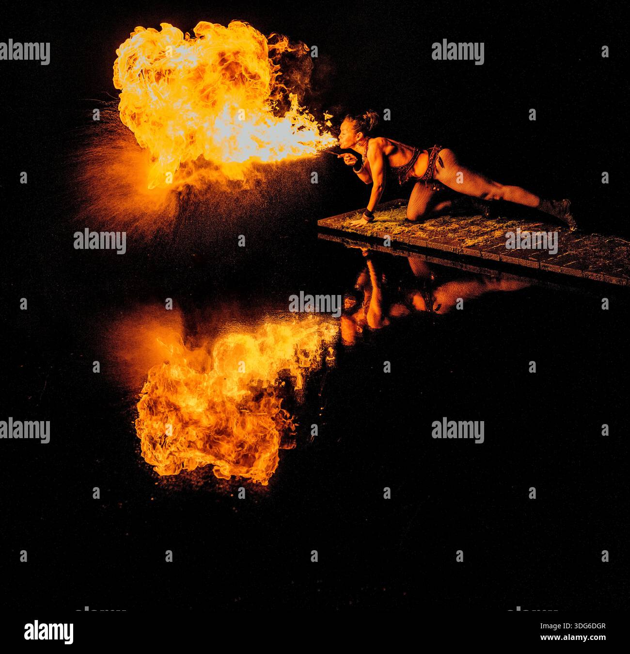 A fire performer breathes flames over a dark body of water at night ...
