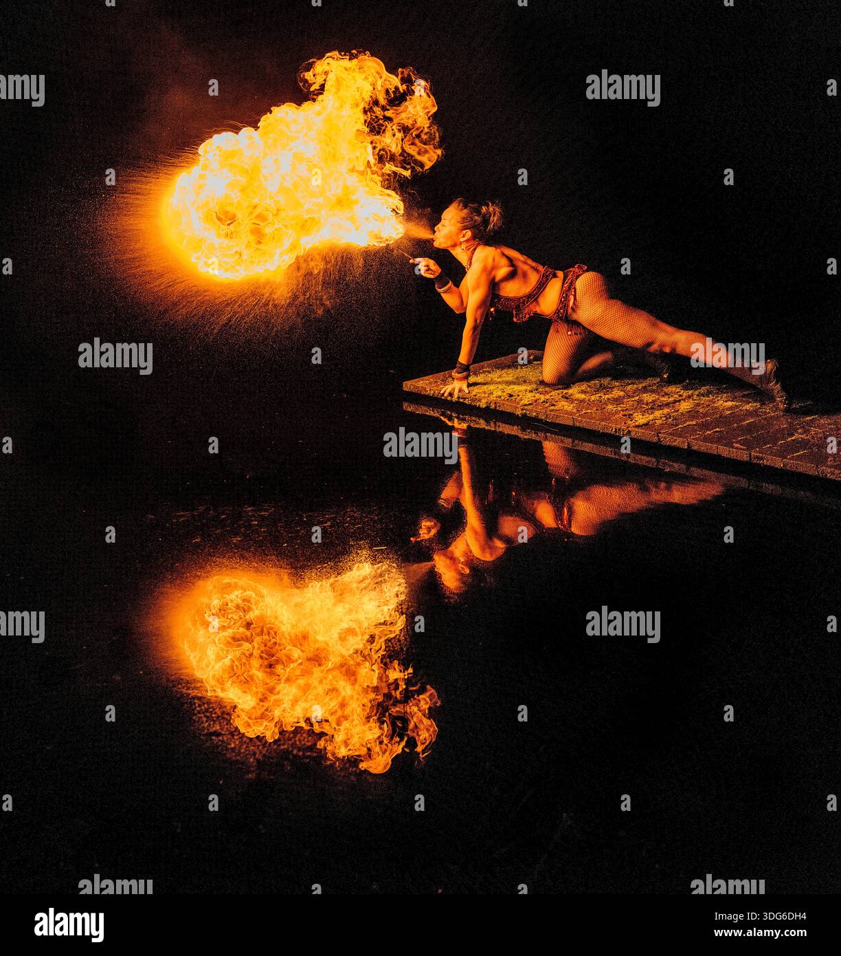 A fire performer breathes flames over a dark body of water at night ...