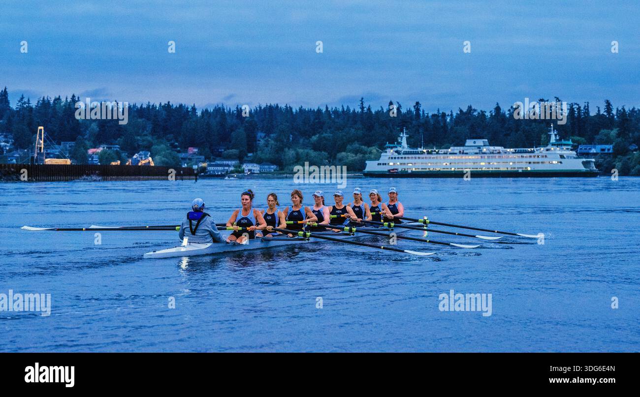 Rowing team practicing in blue water with a forested shoreline and ...