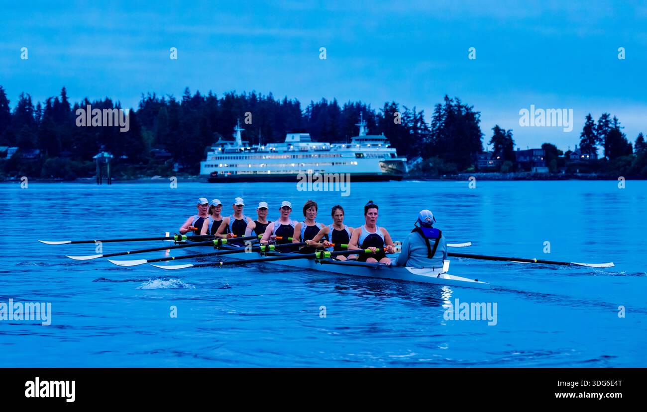 Rowing team practices on a calm lake with a ferry and forested ...