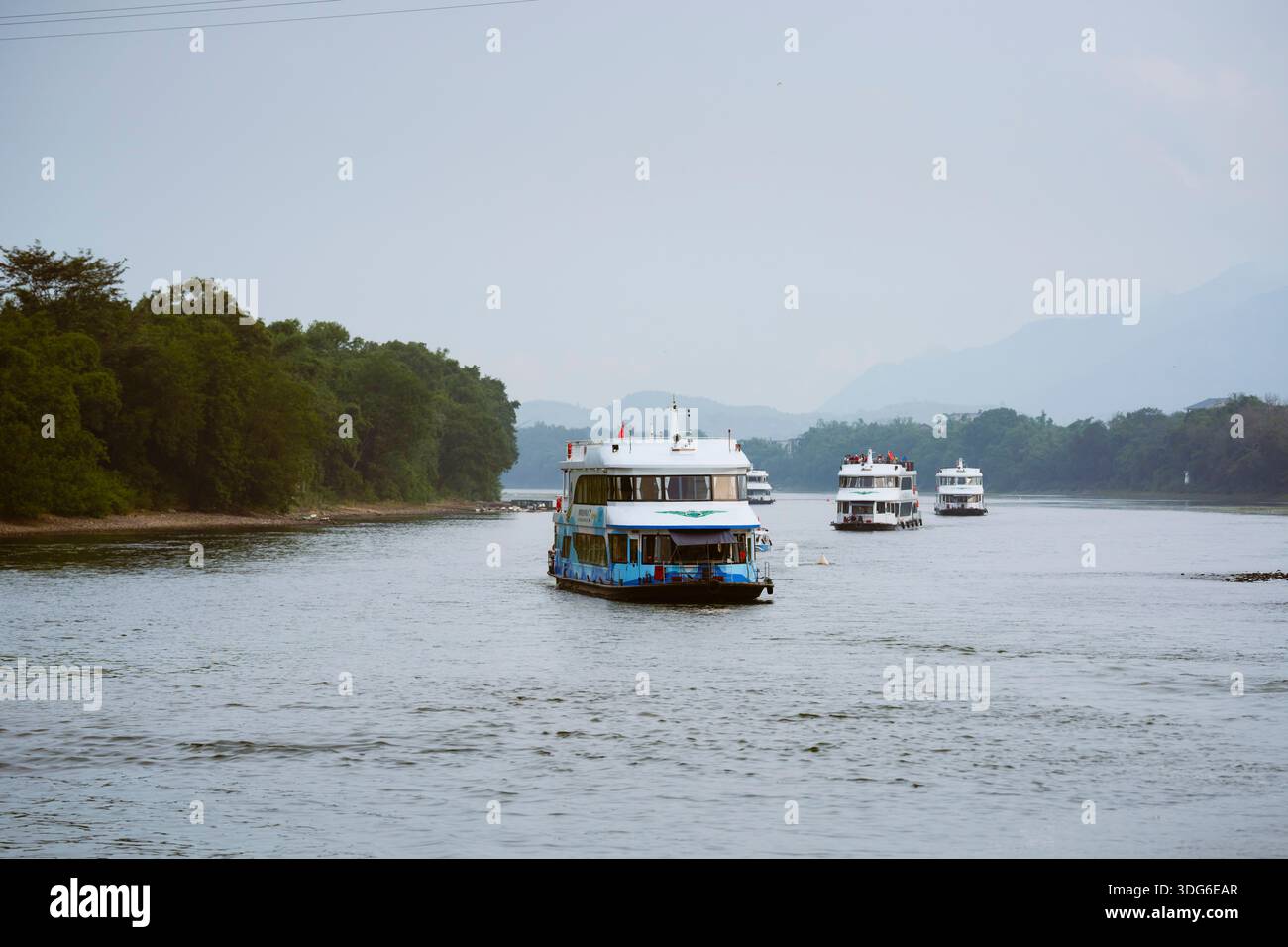 Boats sail along a wide river surrounded by lush greenery and distant ...