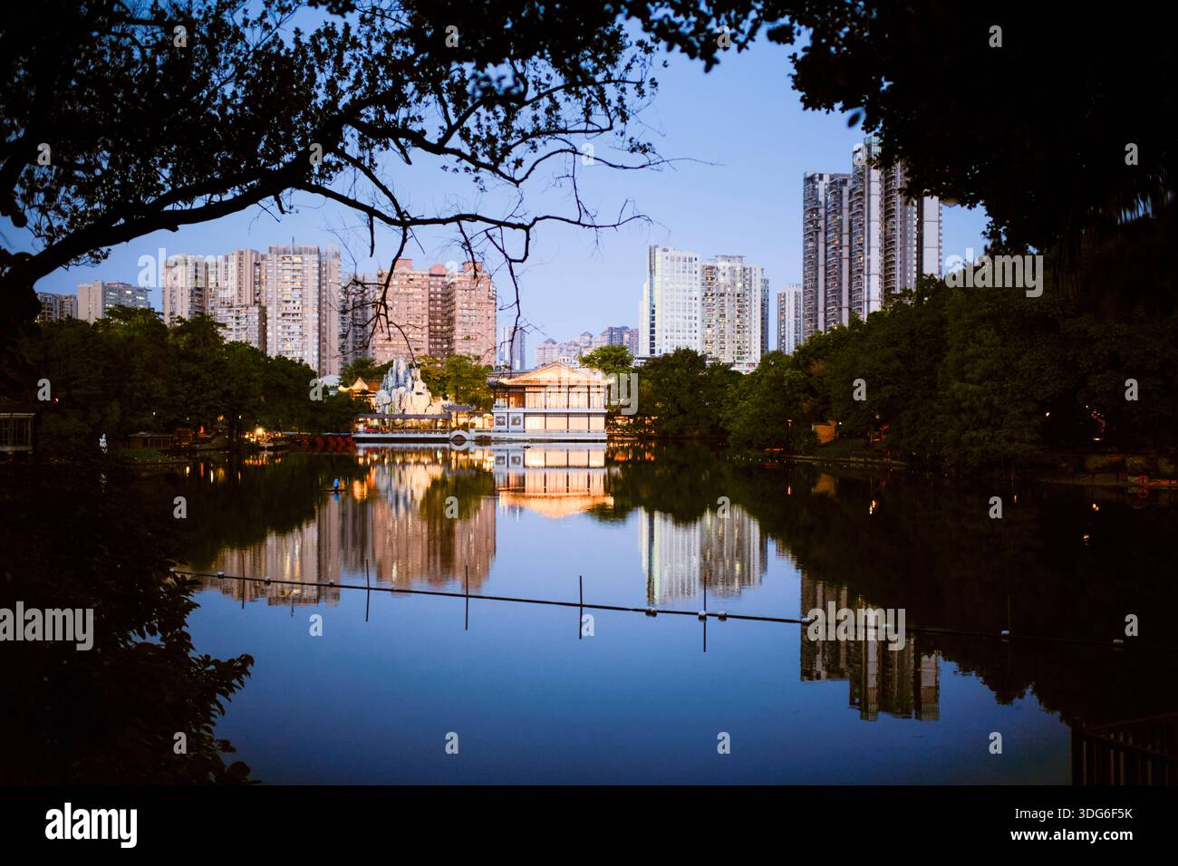 City skyline reflected in a serene lake surrounded by trees at dusk ...