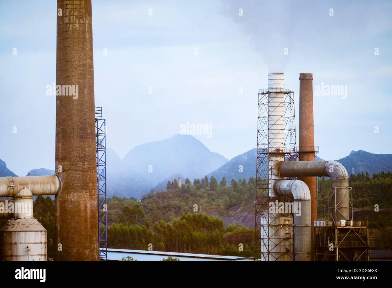 Industrial smokestacks releasing smoke with scenic mountains in the ...