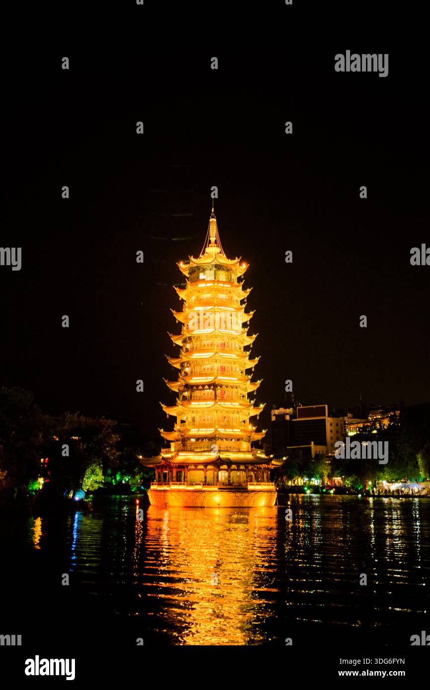 Illuminated pagoda reflecting on the water at night with city lights in ...