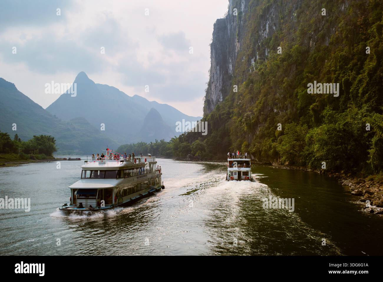 River cruise boats sail between lush green hills and steep cliffs under ...