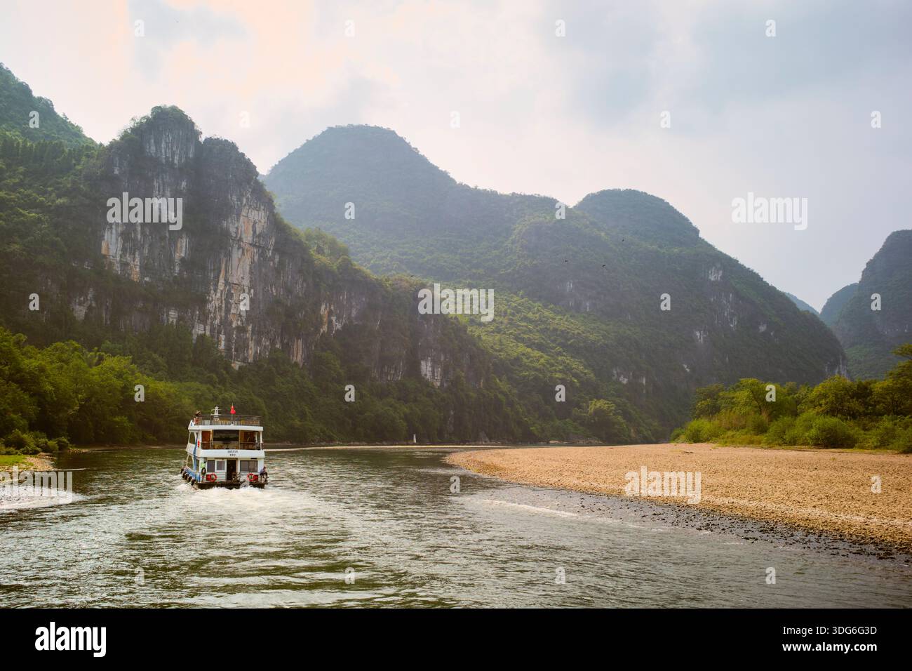 A boat travels along a river surrounded by lush green mountains and ...