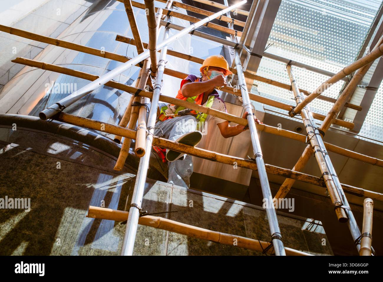 Construction worker climbing bamboo scaffolding on a modern building ...