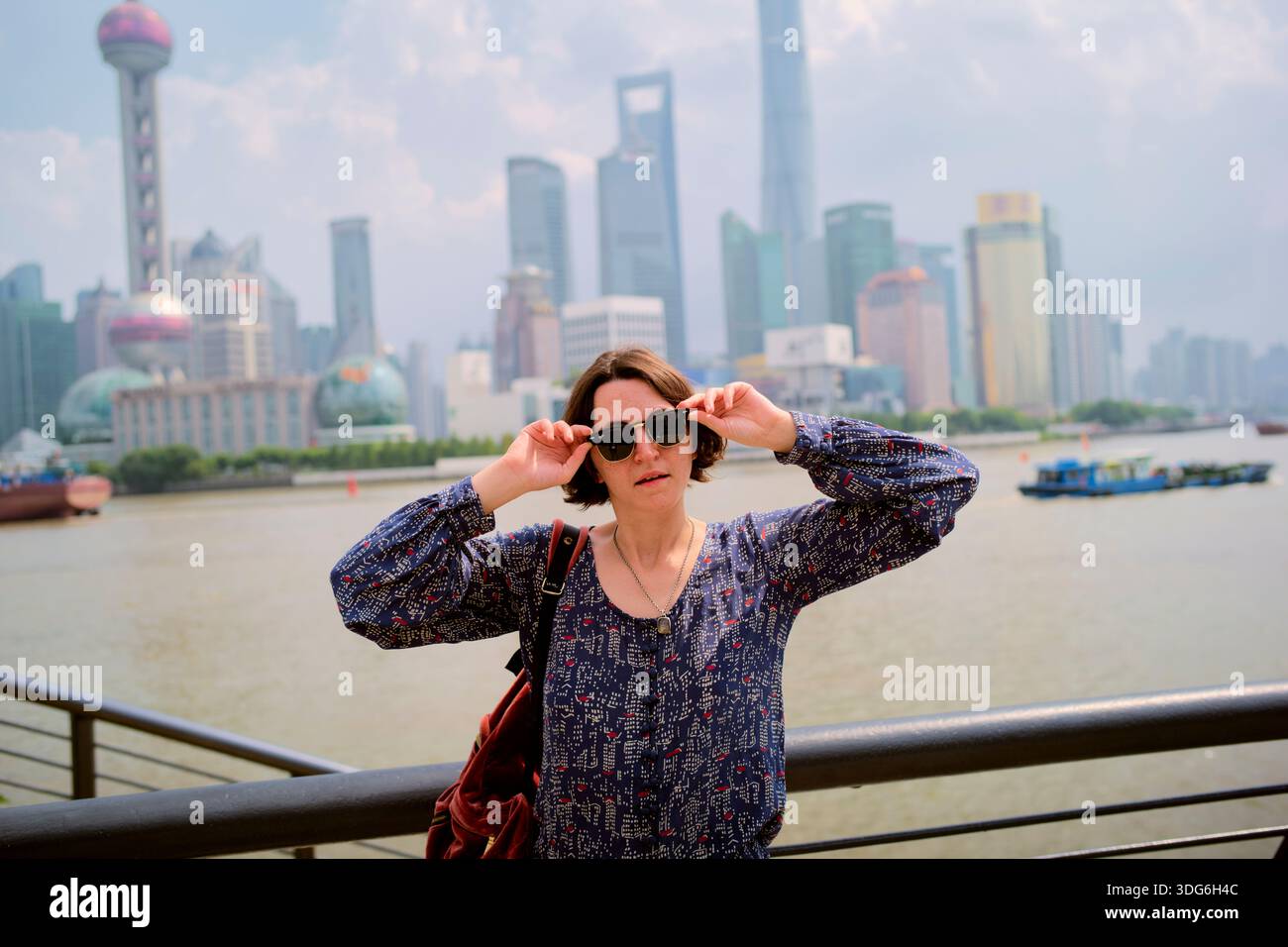 Woman adjusting sunglasses with modern city skyline and river in the ...