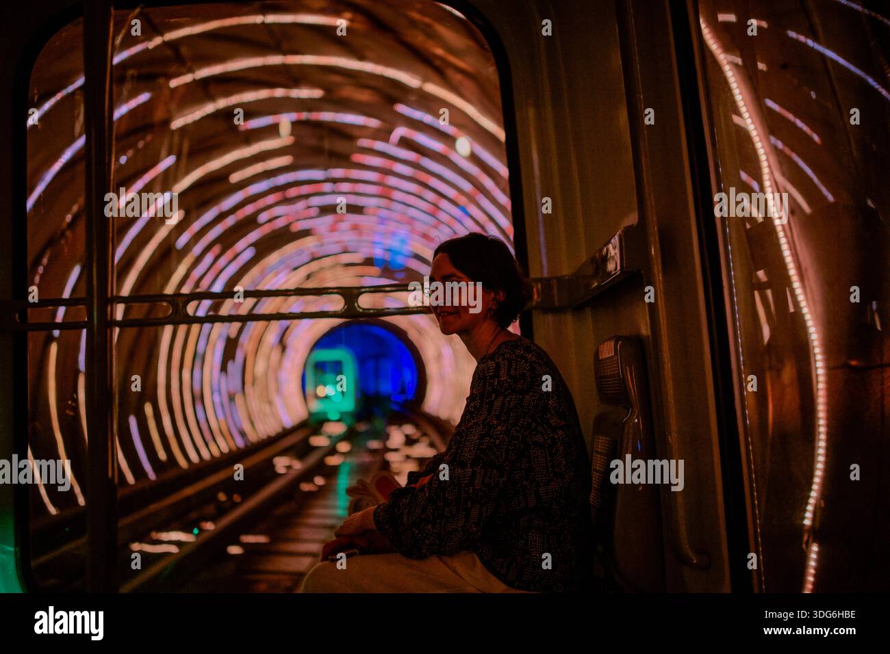 Woman seated inside a tunnel with colorful lights and circular patterns ...