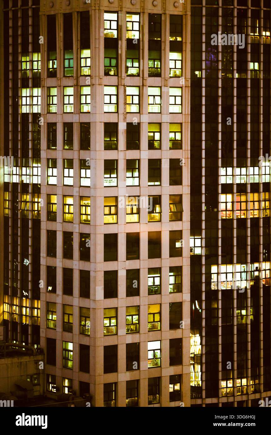 A tall, illuminated office building with glowing windows at night ...