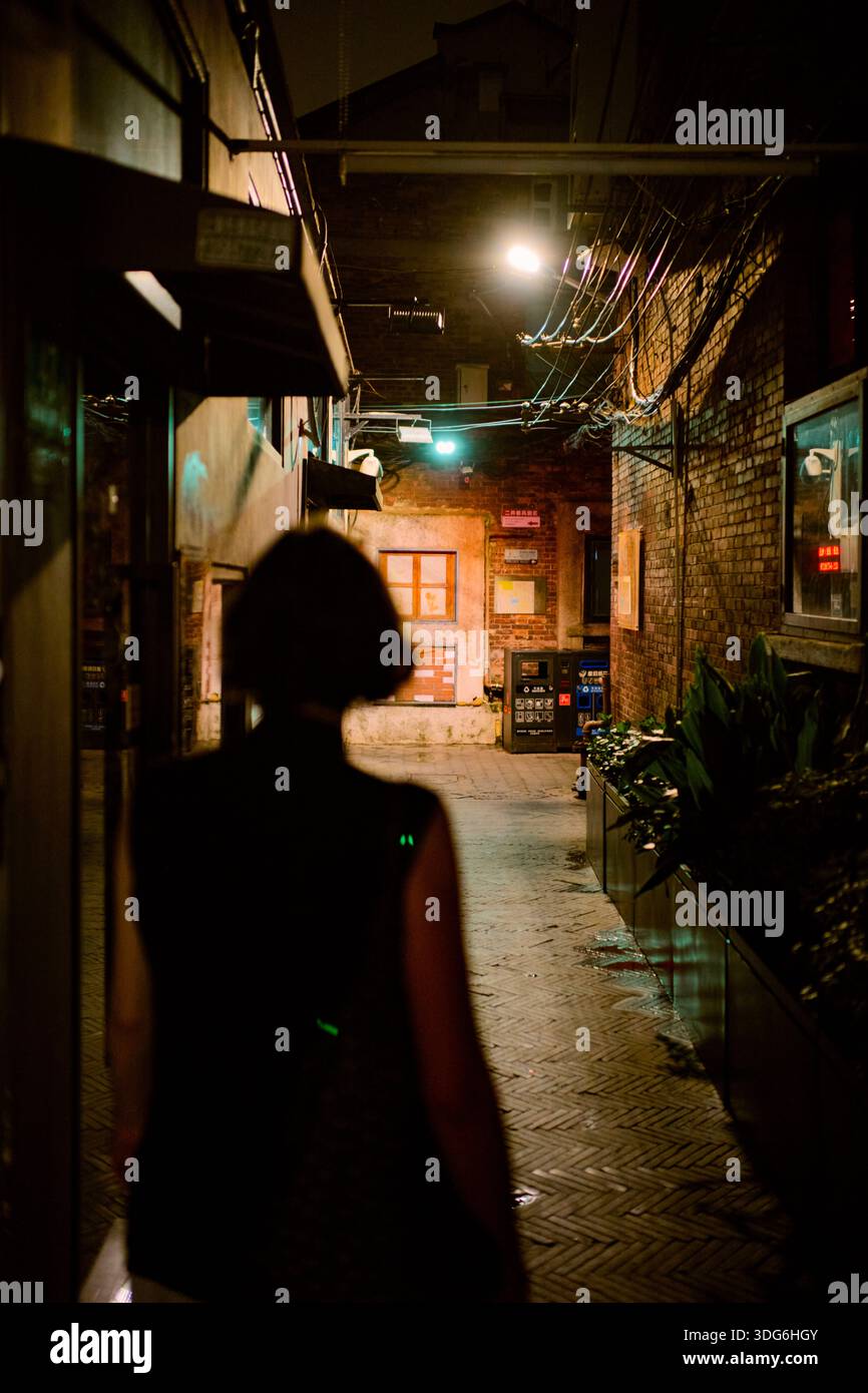 A person walks through a dimly lit urban alley at night with glowing ...