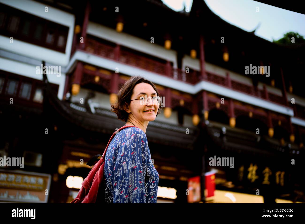 Smiling woman with glasses in a blue blouse with patterns stands ...