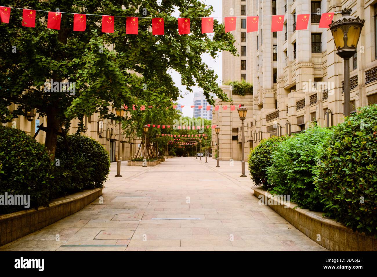 Urban walkway adorned with rows of small red flags, flanked by greenery ...