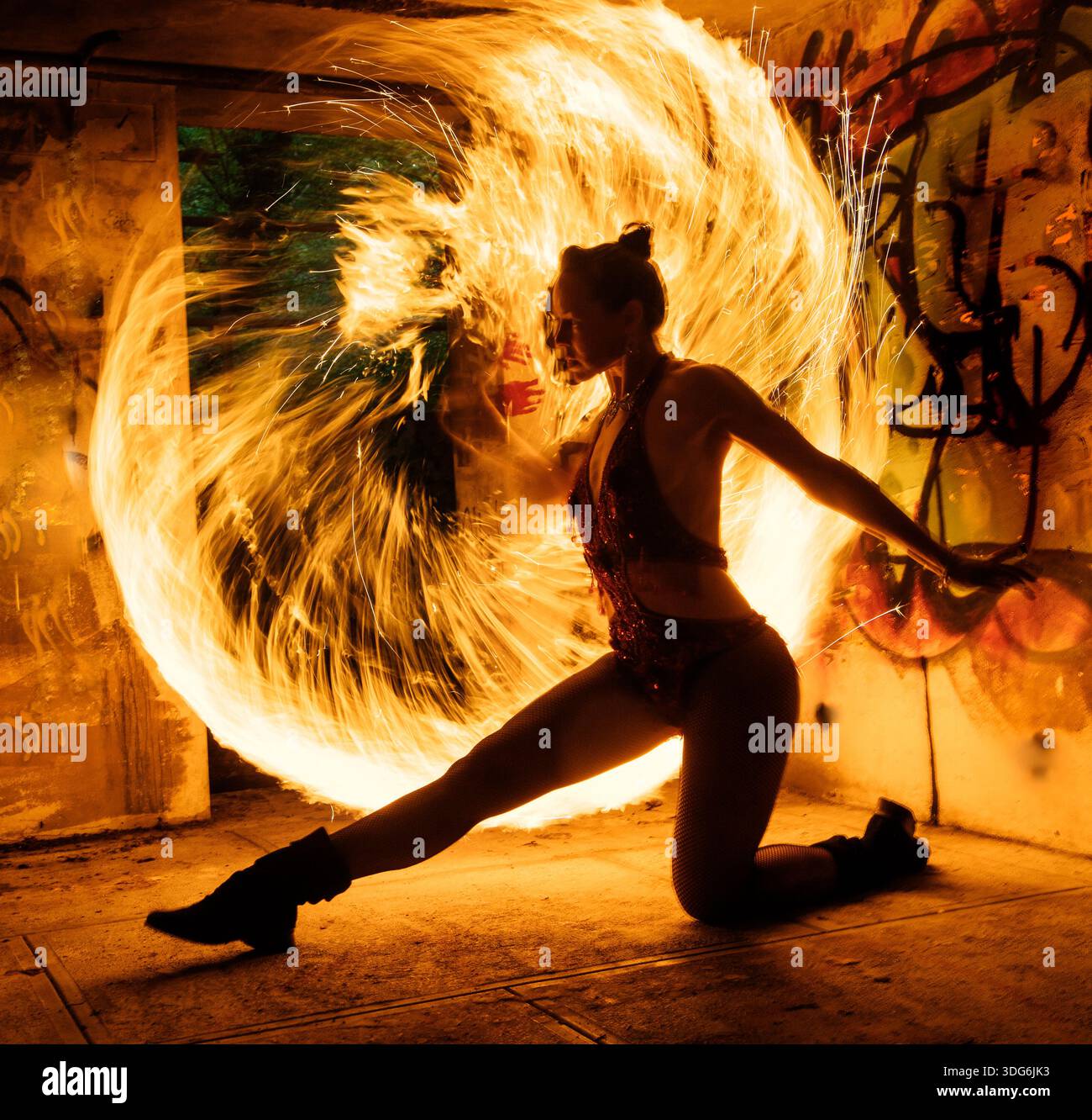 Performer twirls a flaming hoop in a graffiti-covered urban setting at ...