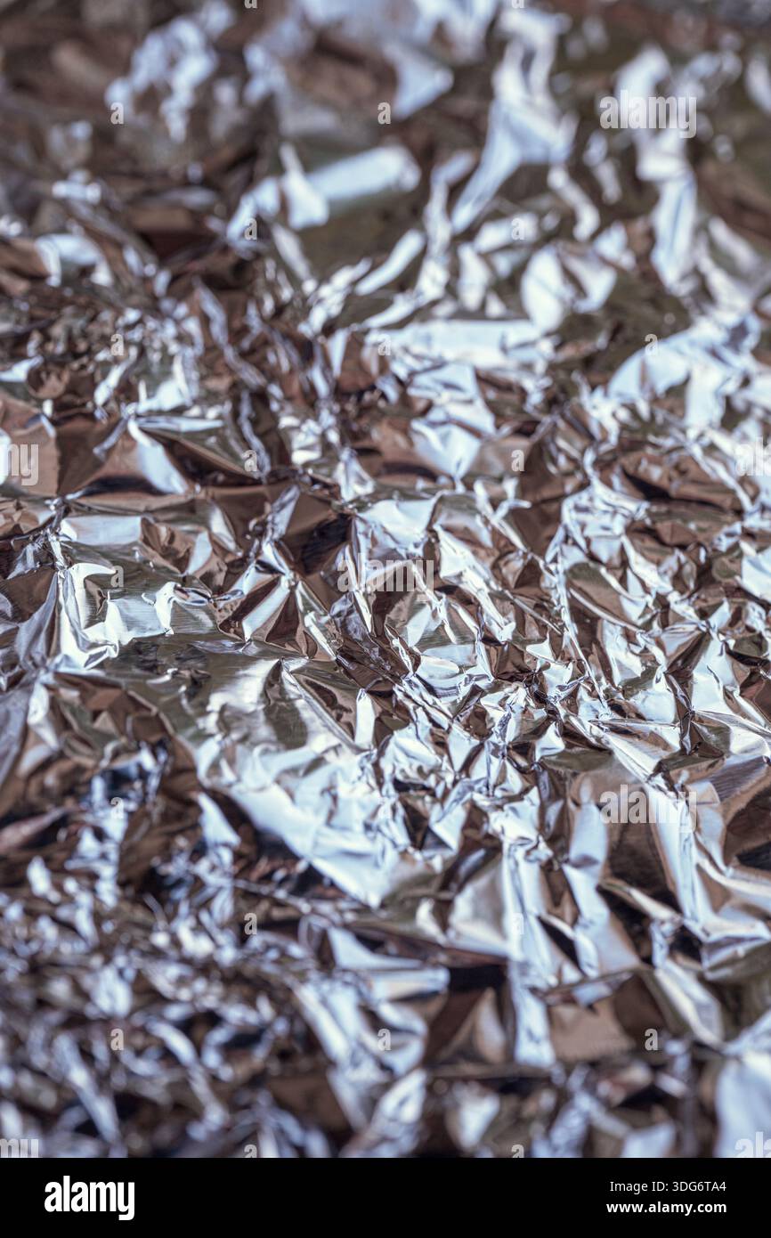 Crumpled aluminum foil reflecting light, creating abstract silver ...