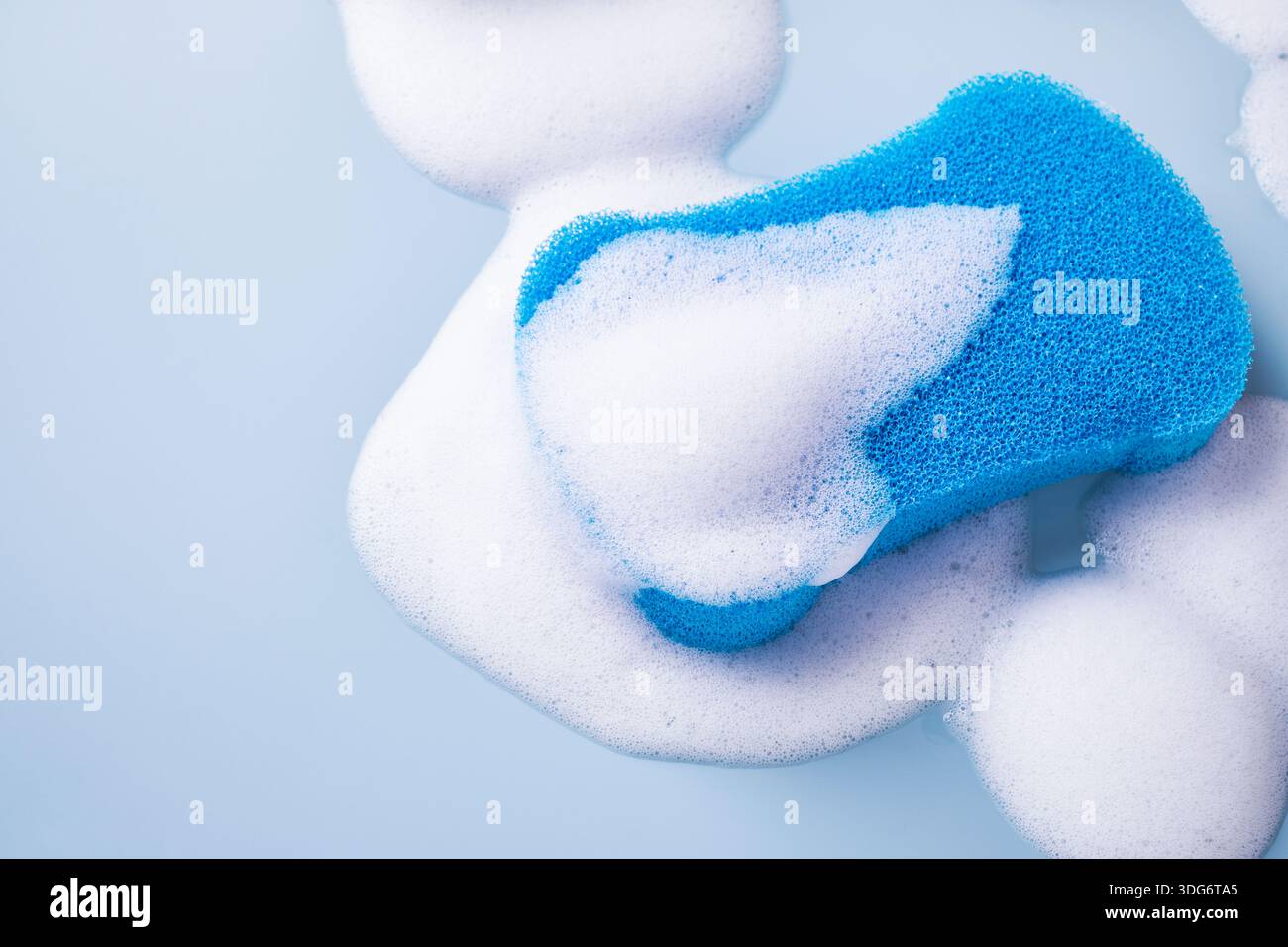 Blue sponge producing white soap foam for cleaning and hygiene on blue ...