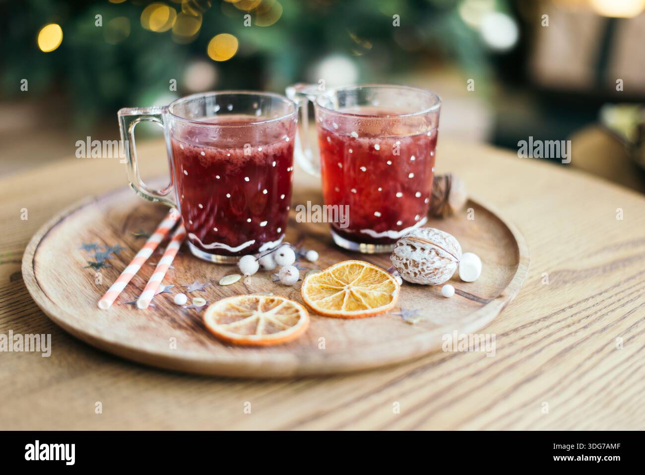 Two glass mugs of red mulled wine on a wooden tray with orange slices ...