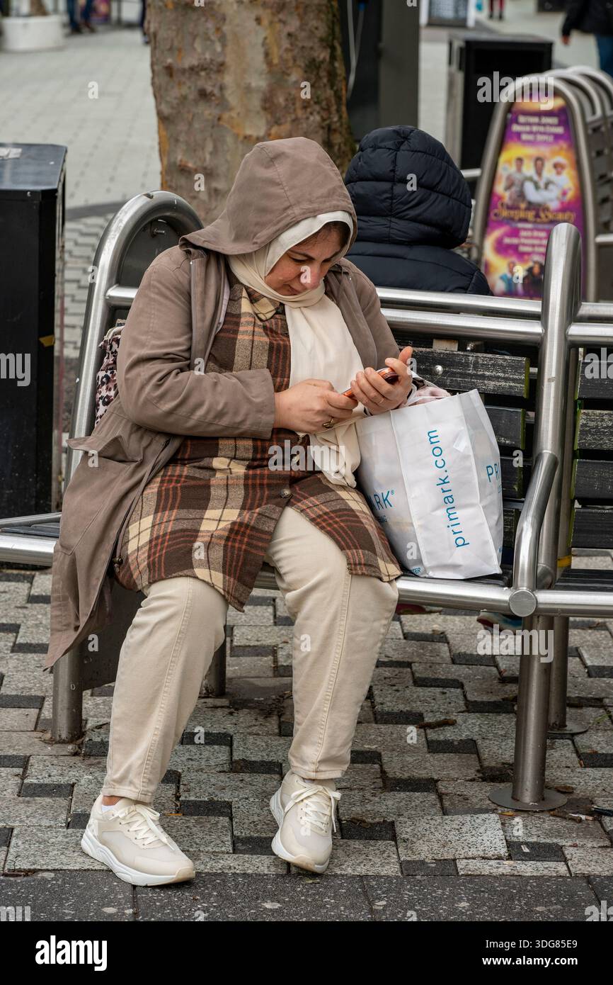 Asian woman wearing winter coat sitting on bench next to a shopping bag ...