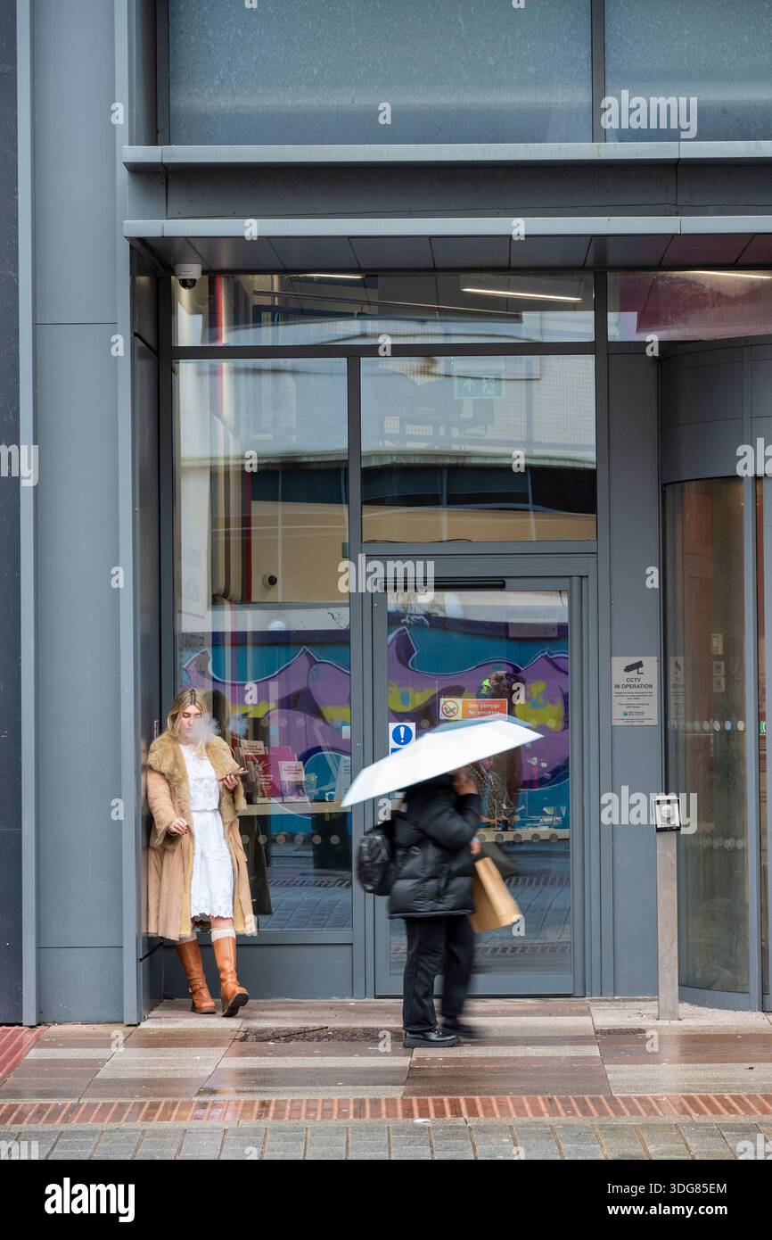 Young woman standing outside of a modern office building smoking a ...