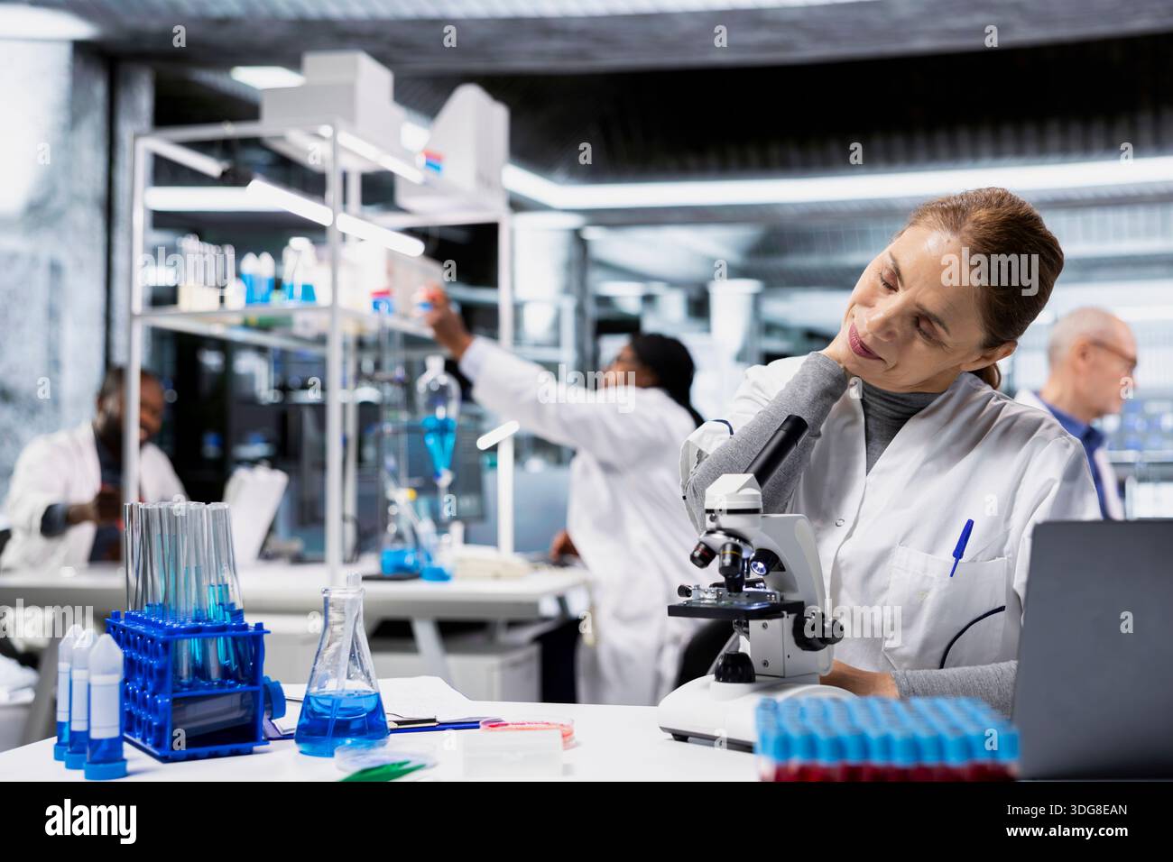 Overworked scientist with neck injury examining stained tissue sections ...
