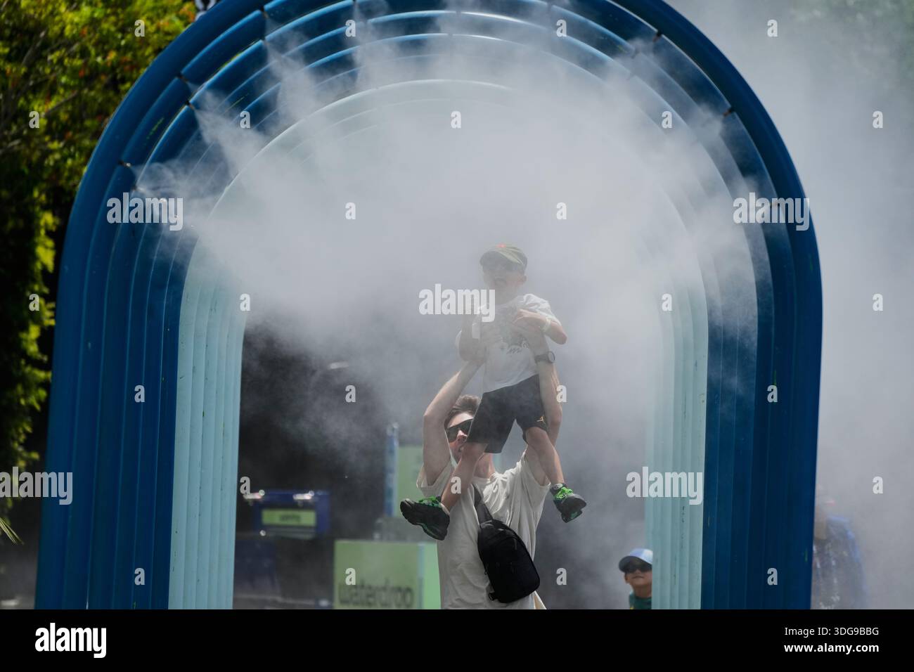 A young boy reacts as he is held up to a water mister to cool down at ...