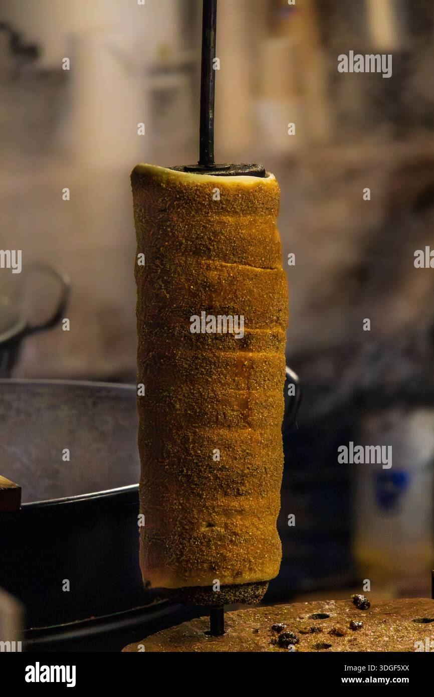 Traditional chimney cake roasting on a vertical spit, coated in sugar ...