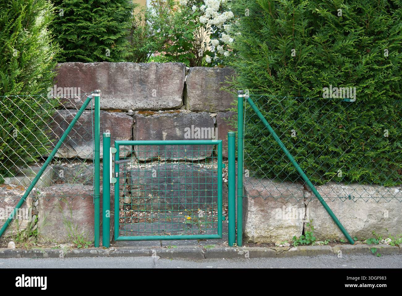 Green metal garden gate set between stone retaining walls, supported by ...