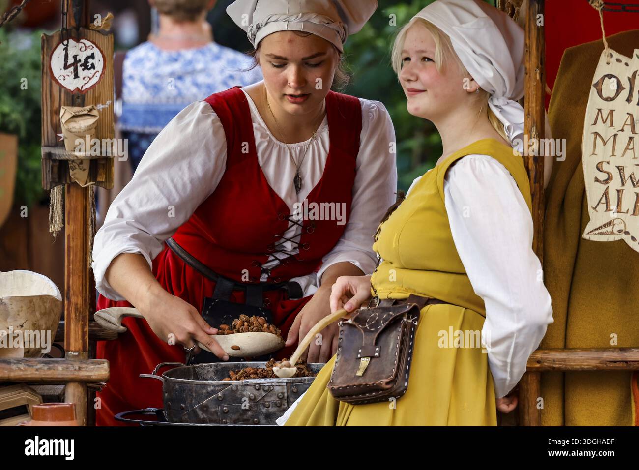 Saleswomen in traditional costumes serve customers at a medieval market ...