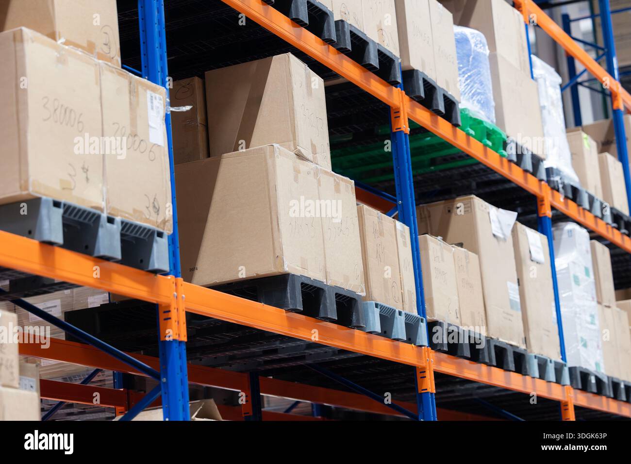 Cardboard boxes are stacked on tall, orange and blue industrial racking ...