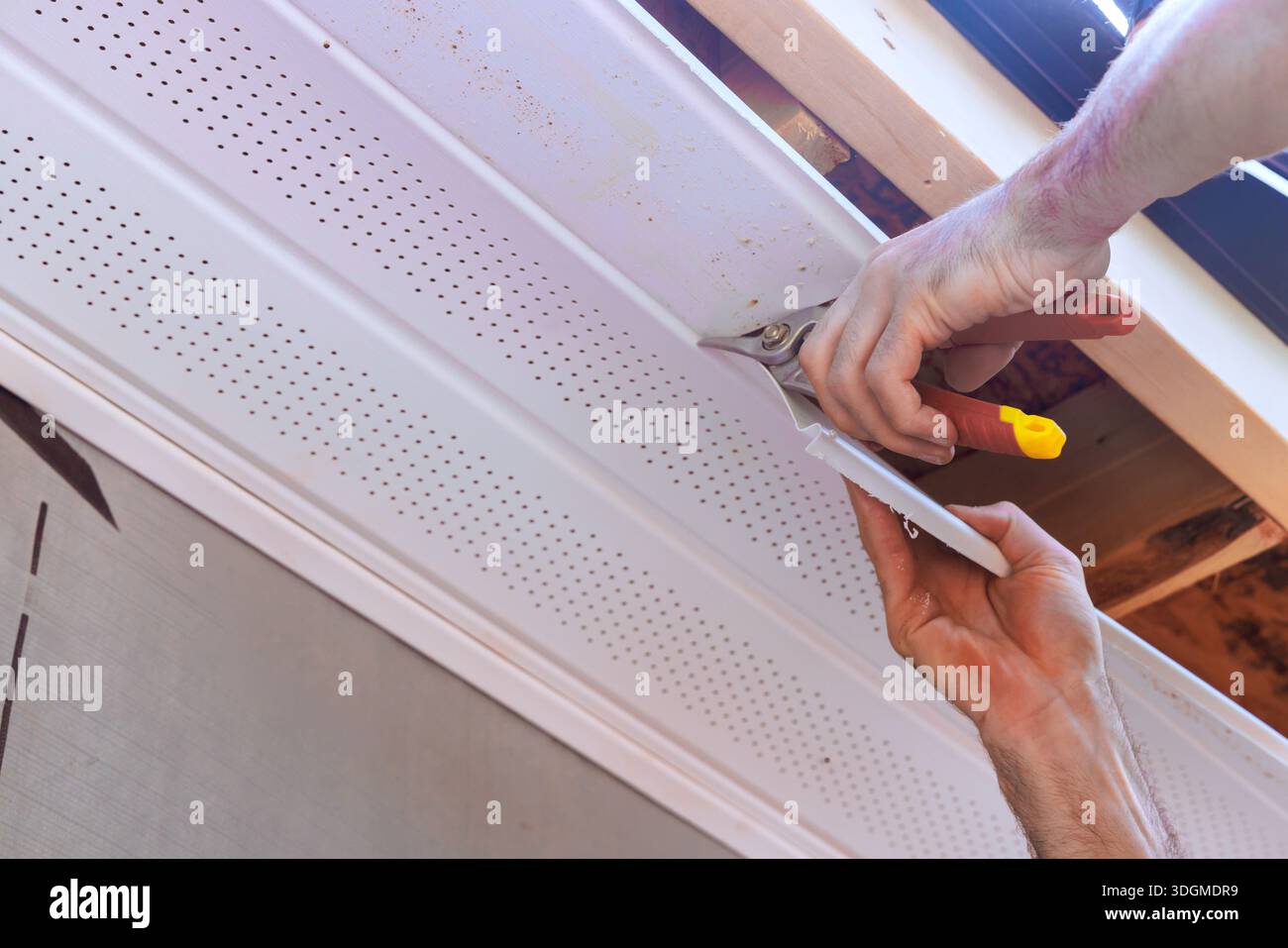 Hands work to fit ceiling soffit panels trim while using cutting tools ...