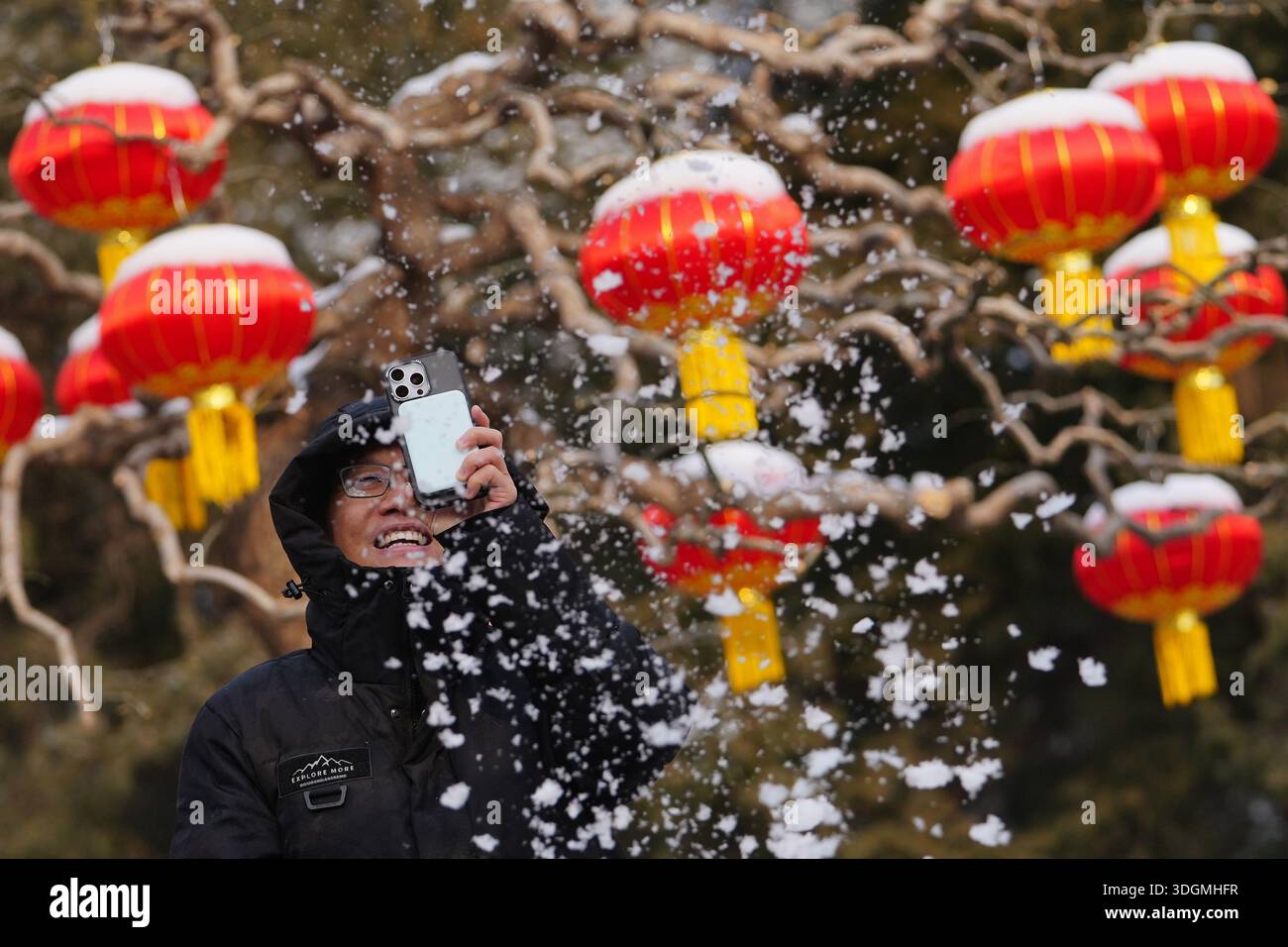 A man films snow falling from a tree decorated with lanterns at the ...