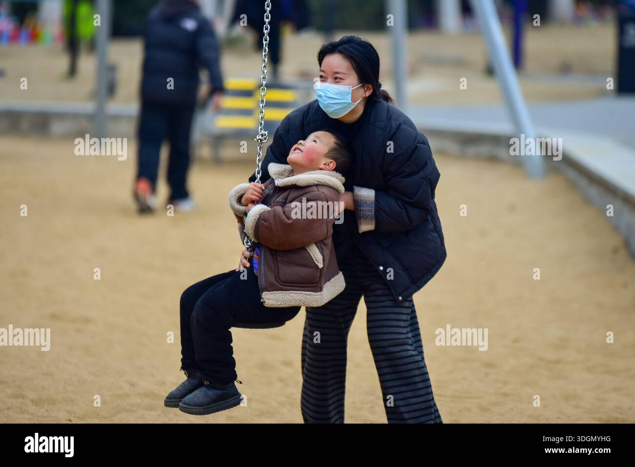 Fuyang City, China. 18th Jan, 2026. A mother wearing a face mask holds ...
