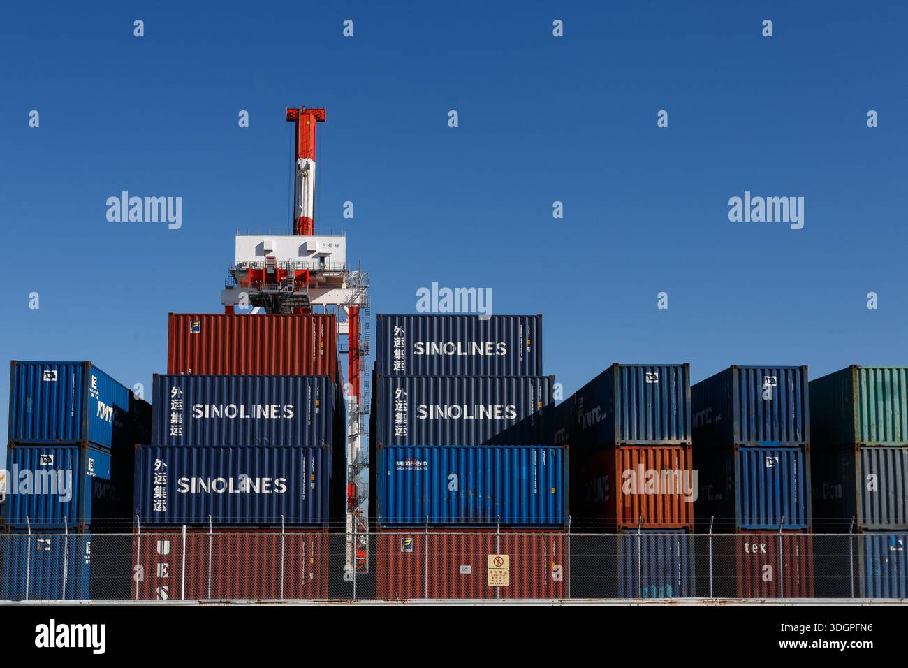 A container crane seen above stacked shipping containers at a wharf on ...
