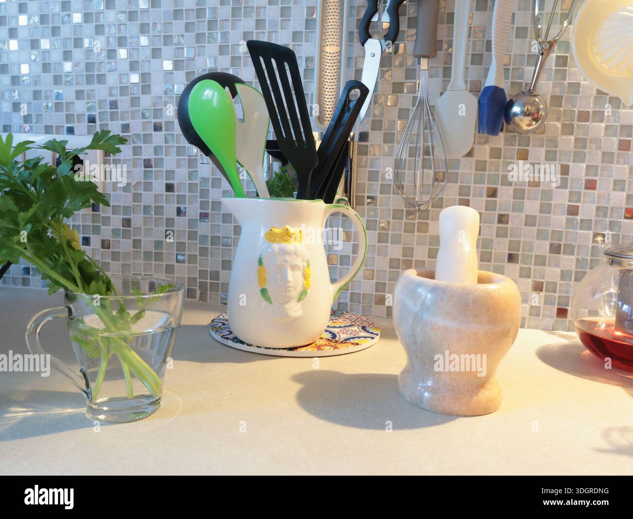 Marble mortar and jug with spoons and spatulas in kitchen. Mosaic tiles ...
