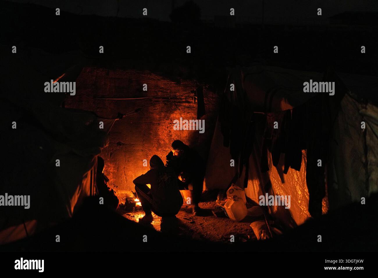 Displaced Palestinians cook and warm themselves around a fire at a tent ...
