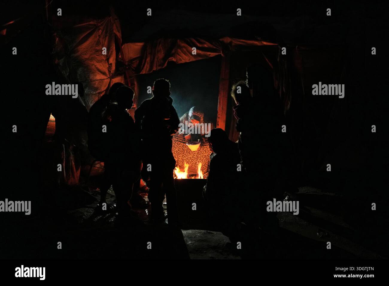 Displaced Palestinians cook and warm themselves around a fire at a tent ...