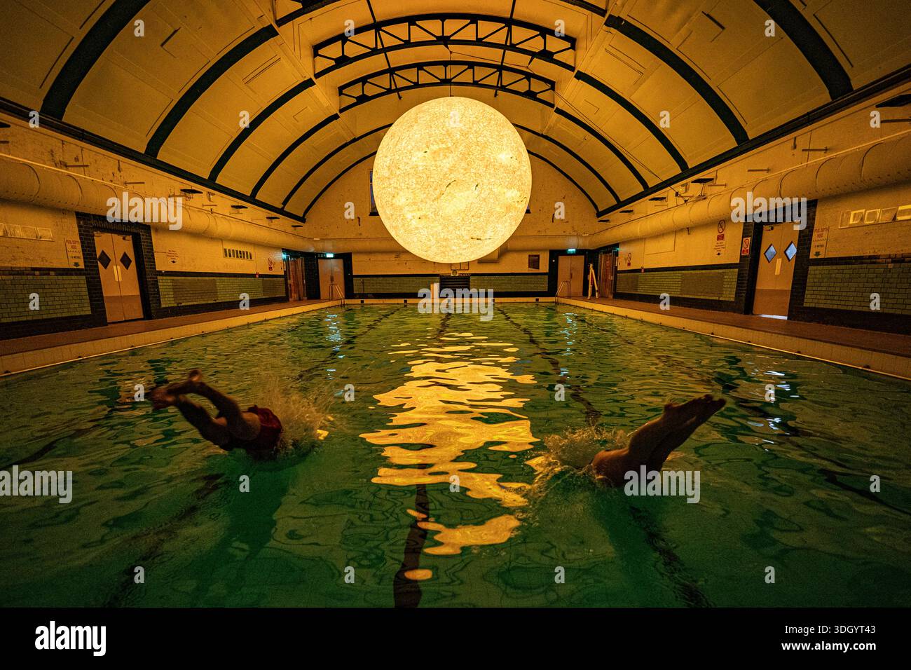 People dive into the water beneath Helios, an illuminated sun ...