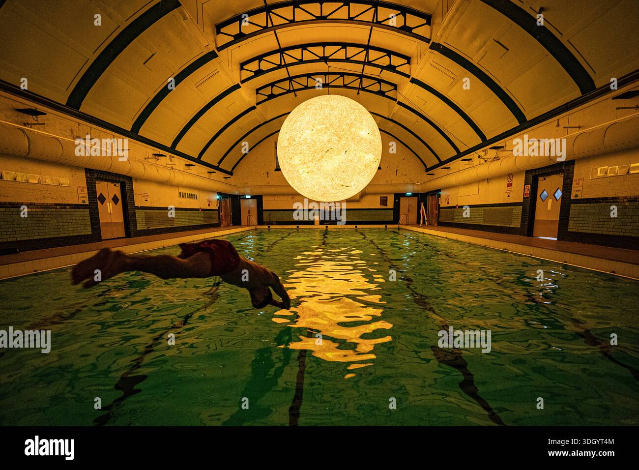 People dive into the water beneath Helios, an illuminated sun ...