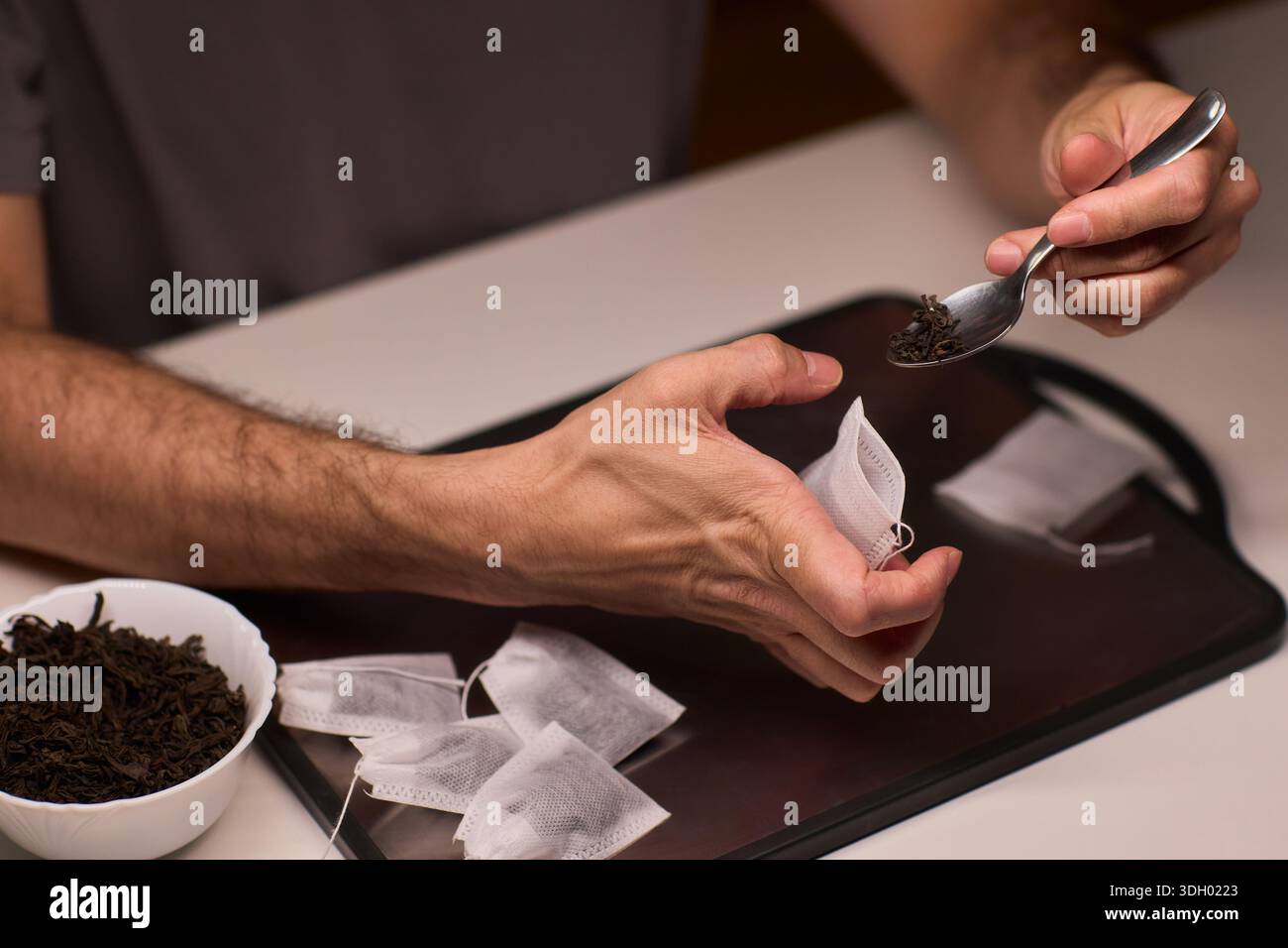 white man filling teabag with loose tea using spoon, bowl of dark ...