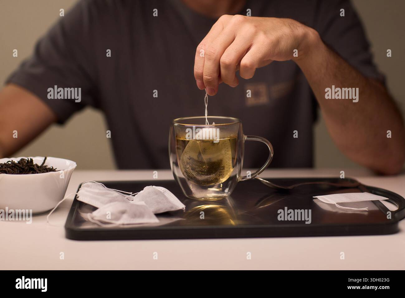 Man steeping green tea bag, hand lowering teabag into clear glass cup ...