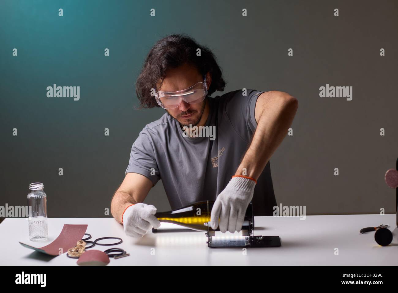 Gloved hands cutting glass bottle on bench, rotary cutter mounted in ...